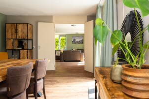 Uma sala de estar moderna com uma mesa de jantar de madeira, cadeiras de couro, um sofá e uma planta grande.
