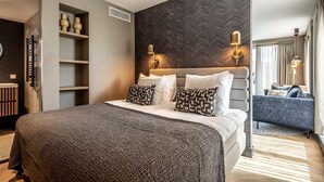 Quarto moderno com uma cama grande, duas luminárias fixadas na parede, uma estante embutida e um sofá cinzento no canto.