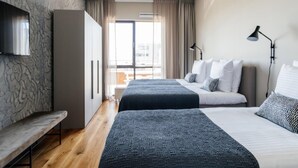 Quarto de hotel moderno com uma cama grande, um banco, uma TV e vista da cidade pela janela.
