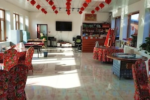 Um hall de hotel com balcão de recepção, área de estar e uma televisão na parede.