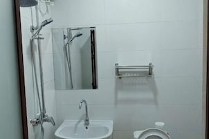 Casa de banho com lavatório, espelho, chuveiro e sanita.