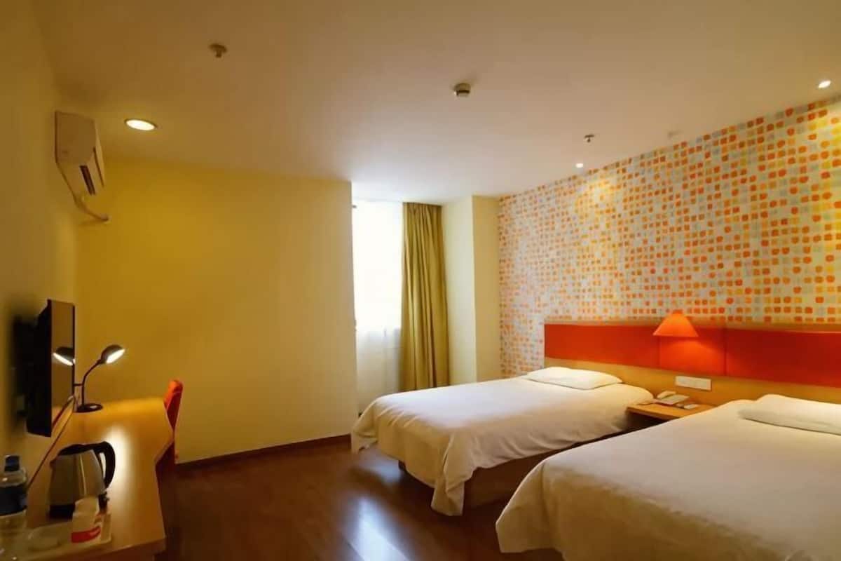 Quarto de hotel com duas camas, uma escrivaninha com luminária, televisão e janela com cortinas.