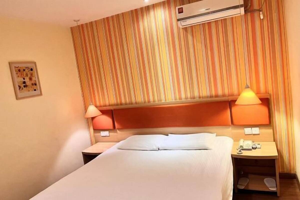 Quarto de hotel com cama, duas luminárias de cabeceira, mesa de cabeceira, ar-condicionado e parede listrada.