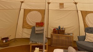 Uma tenda com um poste central, uma mesa pequena com objetos e uma cadeira.