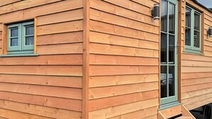 Uma casa móvel de madeira com telhado curvo, porta deslizante e um pequeno lance de escadas que levam à entrada.