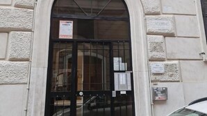 Fachada de edifício com uma grande entrada em arco, um portão de metal preto e uma placa indicando um condomínio.