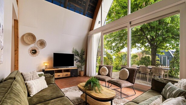 Uma sala de estar moderna com uma TV grande, assentos confortáveis e vista para o exterior.