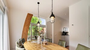 Uma mesa de jantar oval de madeira com cadeiras, um lustre pendente e vista para o exterior.