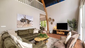 Uma sala de estar espaçosa com teto alto, uma pintura grande, uma TV de tela plana e um confortável arranjo de assentos.