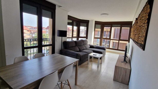 Uma sala de estar moderna com um sofá, uma mesa de jantar e grandes janelas com vista para edifícios.