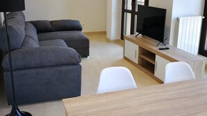 Uma sala de estar moderna com um sofá cinzento, uma mesa de centro de madeira, uma TV em um móvel e uma cadeira branca.