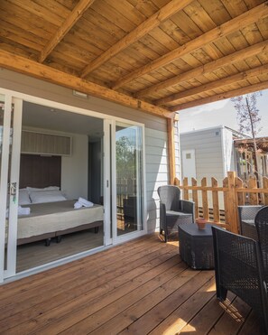 Um deck de madeira com uma porta de correr de vidro que dá para um quarto com uma cama e uma mesinha.