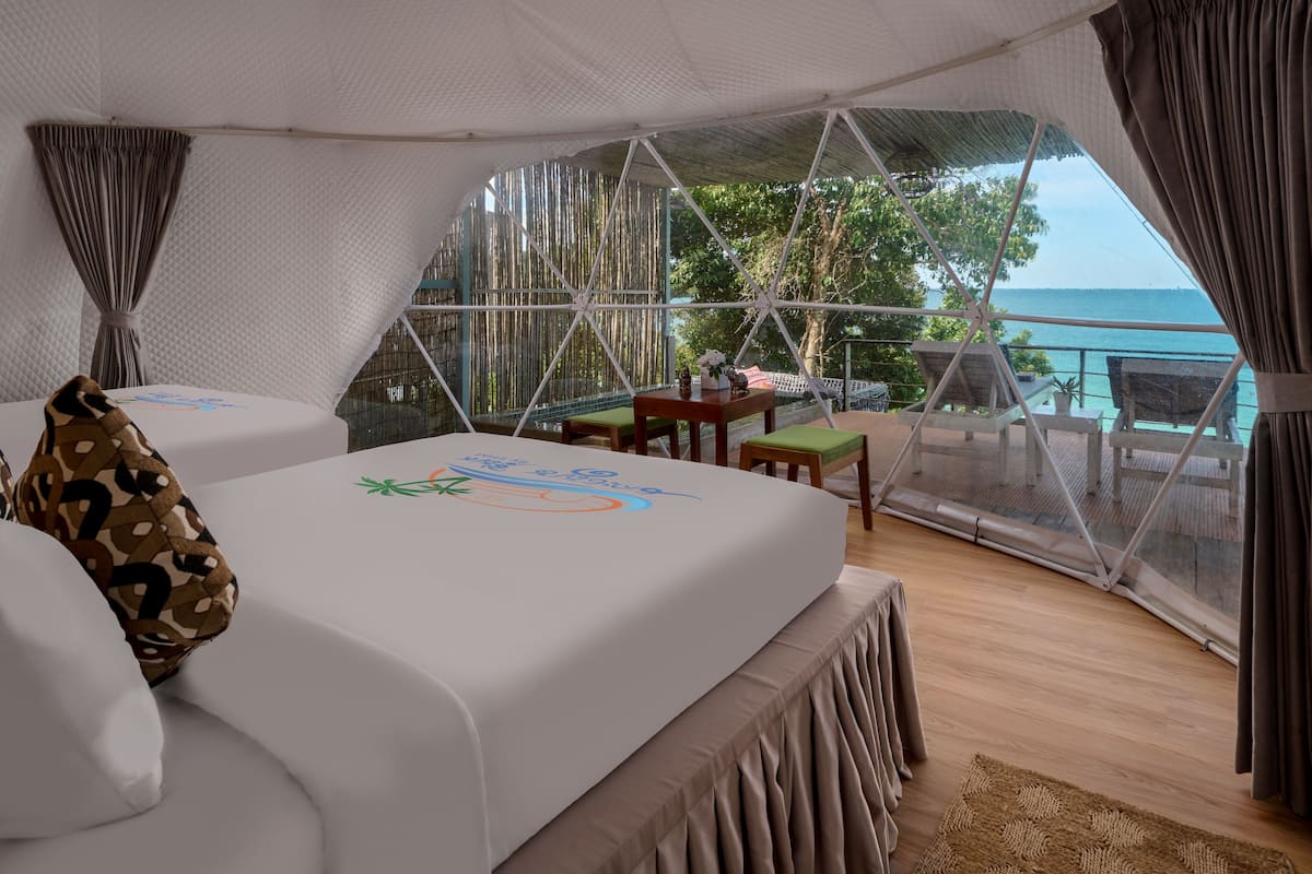 Um quarto com tenda, duas camas, uma mesinha e vista para o oceano.