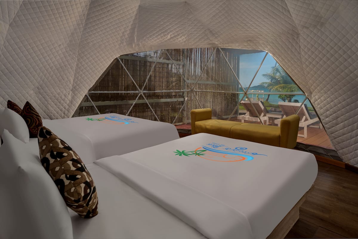 Quarto tipo tenda com duas camas, uma cadeira amarela e vista para a praia.