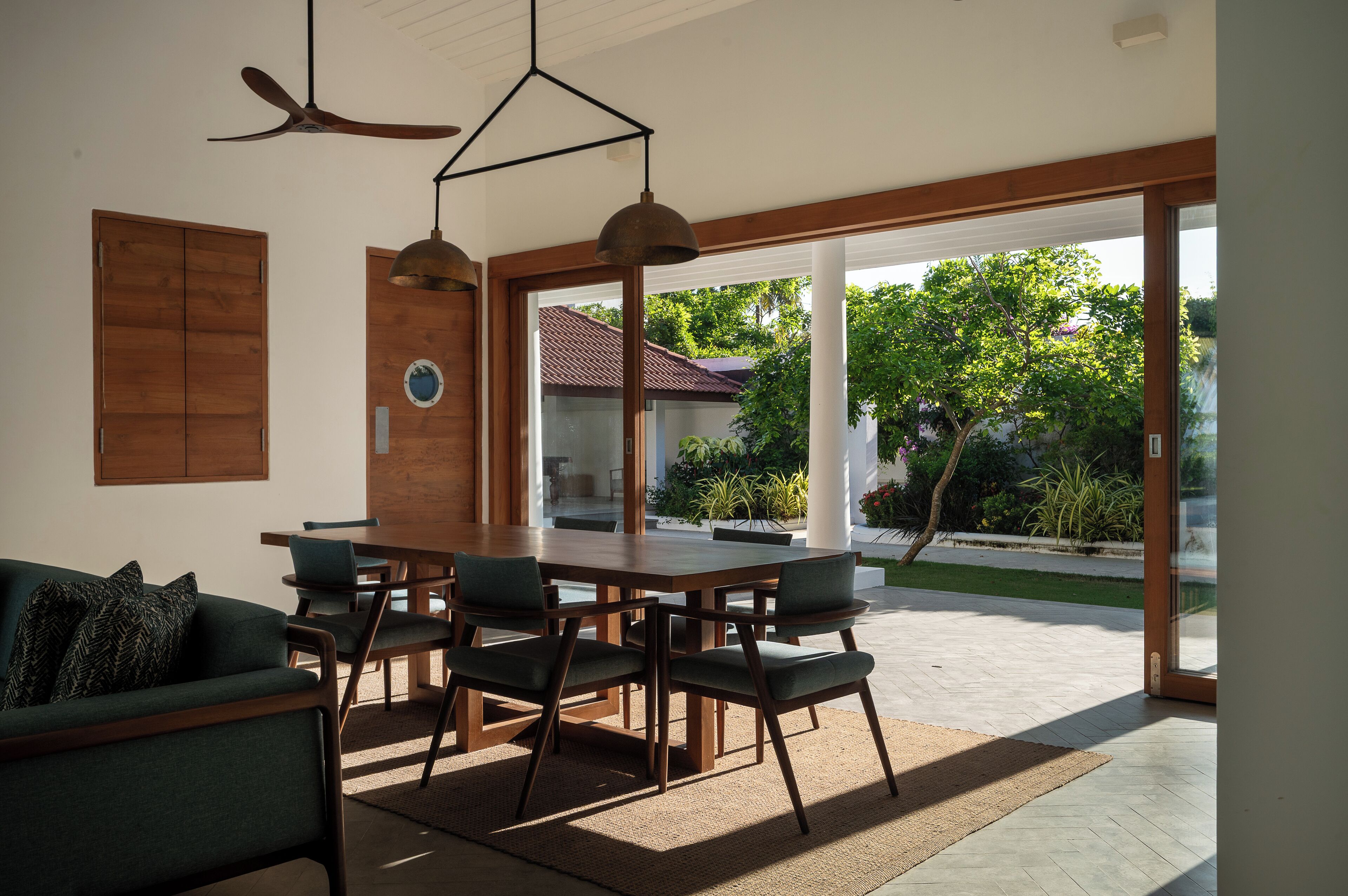 Uma sala de jantar moderna com uma mesa e cadeiras de madeira, um sofá verde e um ventilador de teto.