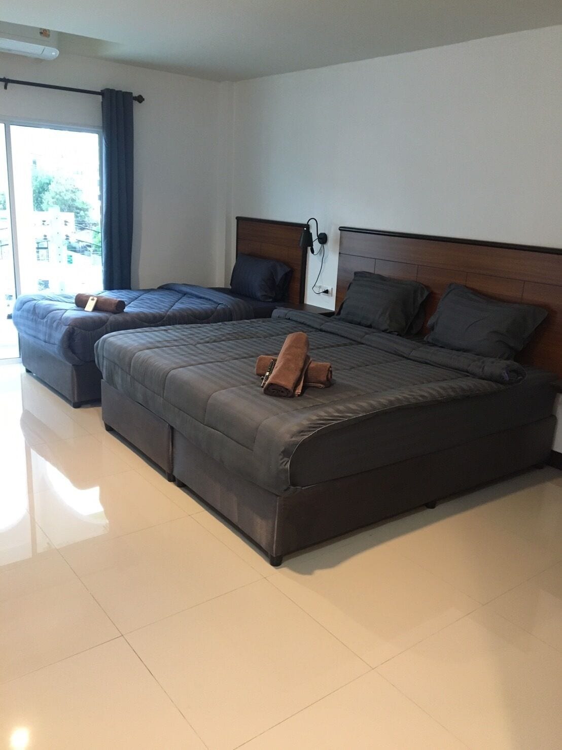 Quarto de hotel com duas camas, uma janela grande com cortinas, televisão de tela plana e mesa de cabeceira com abajur.