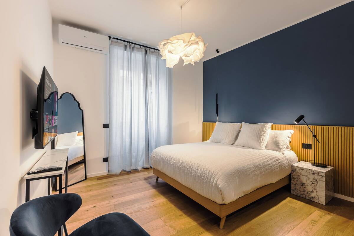 Quarto moderno com cama grande, escrivaninha, cadeira e luminária original.