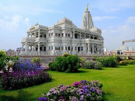 Um templo grande e ornamentado, com esculturas detalhadas e múltiplas torres, rodeado por jardins bem cuidados e um céu claro.