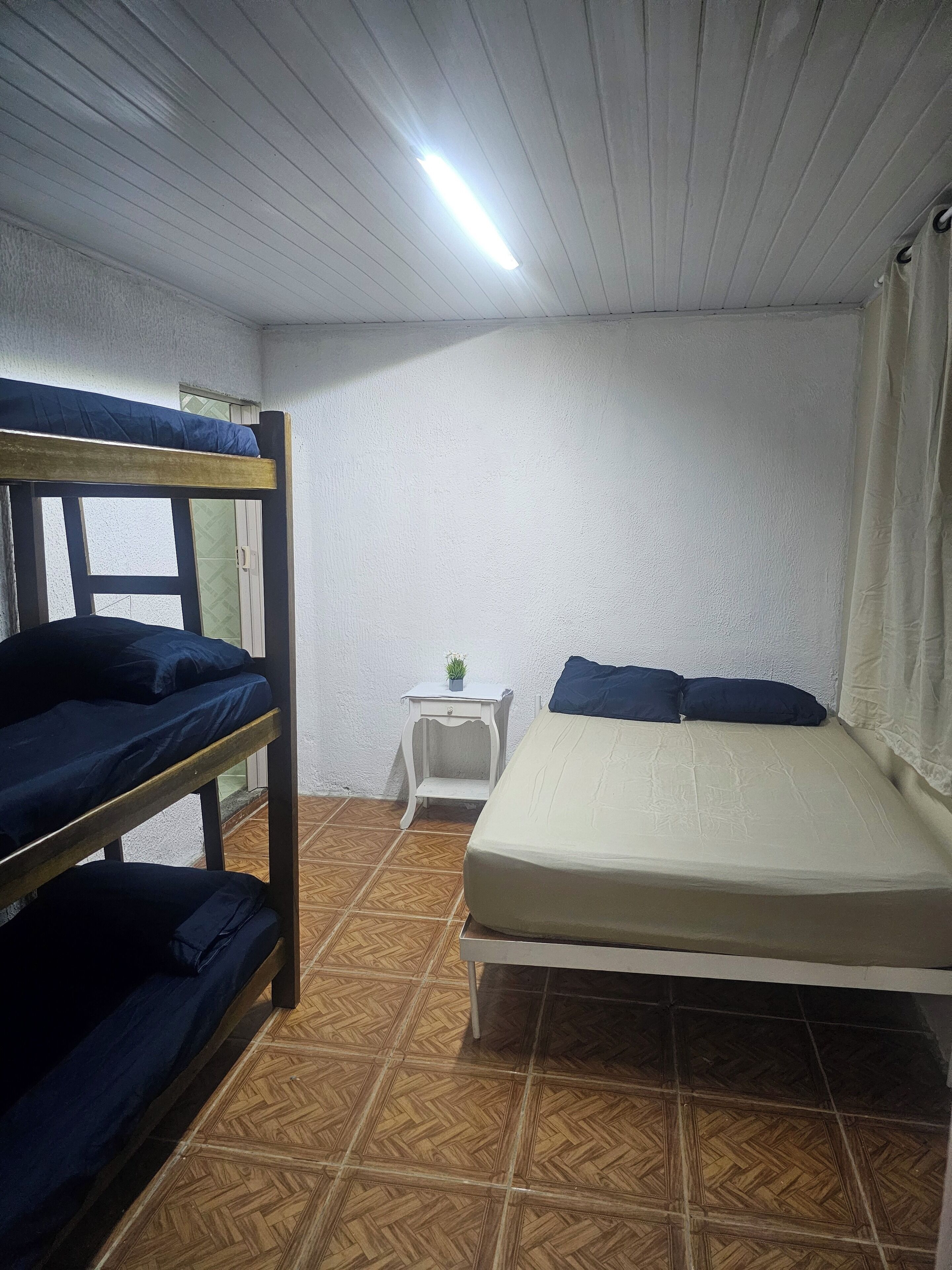 Quarto com uma cama de solteiro, uma cama individual, uma mesinha com uma planta e uma janela com vista.