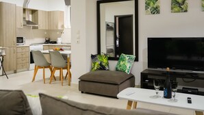 Uma cozinha moderna com armários de madeira, uma sala de jantar com mesa e cadeiras, um sofá, uma televisão e um espelho.