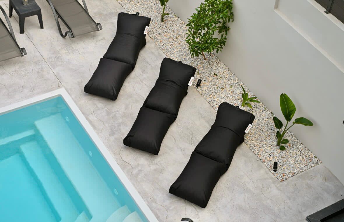 Área de piscina no terraço com cadeiras de sol pretas e uma pequena planta.