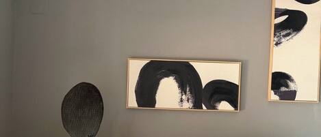 Quarto moderno com escrivaninha de madeira, cadeira cinza, luminária pendente e arte abstrata na parede.