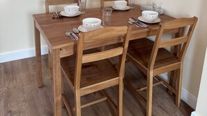 Uma mesa de jantar com quatro cadeiras, louça branca e talheres.