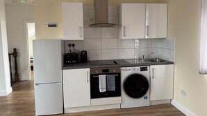 Uma cozinha compacta com armários brancos, forno embutido, máquina de lavar e torradeira.