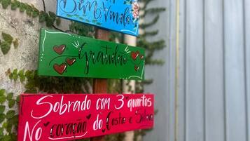 Três placas de madeira com mensagens em português, fixadas em uma parede coberta de hera verde.