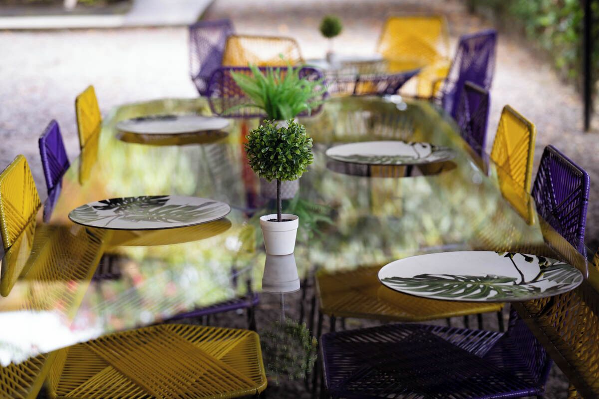 Uma área de refeições com mesas e cadeiras redondas, algumas com estofamento amarelo e roxo.