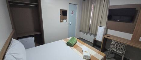 Quarto de hotel com cama, escrivaninha, televisão e guarda-roupa.