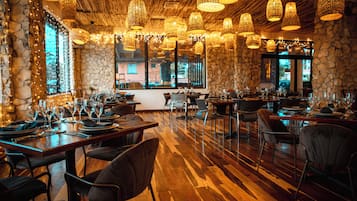 Um restaurante com piso de madeira, paredes de pedra e várias mesas dispostas com taças de vinho e pratos.