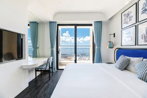 Quarto de hotel com cama, escrivaninha, cadeira, televisão e varanda com vista para o mar.