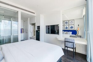 Quarto de hotel moderno com uma cama grande, uma escrivaninha com cadeira, um espelho e vista para a varanda.