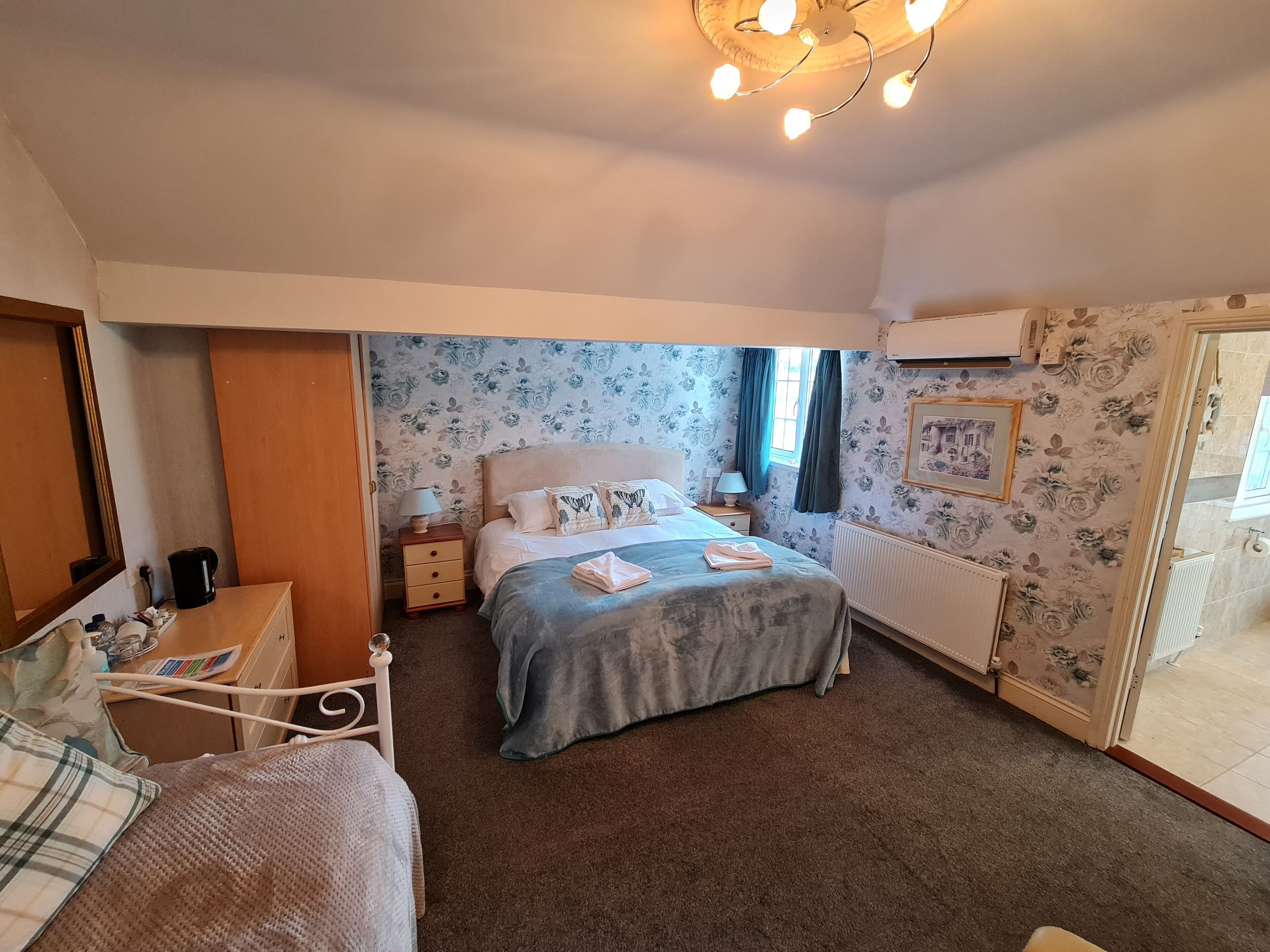 Quarto com cama, mesas de cabeceira, cômoda, radiador e papel de parede floral.