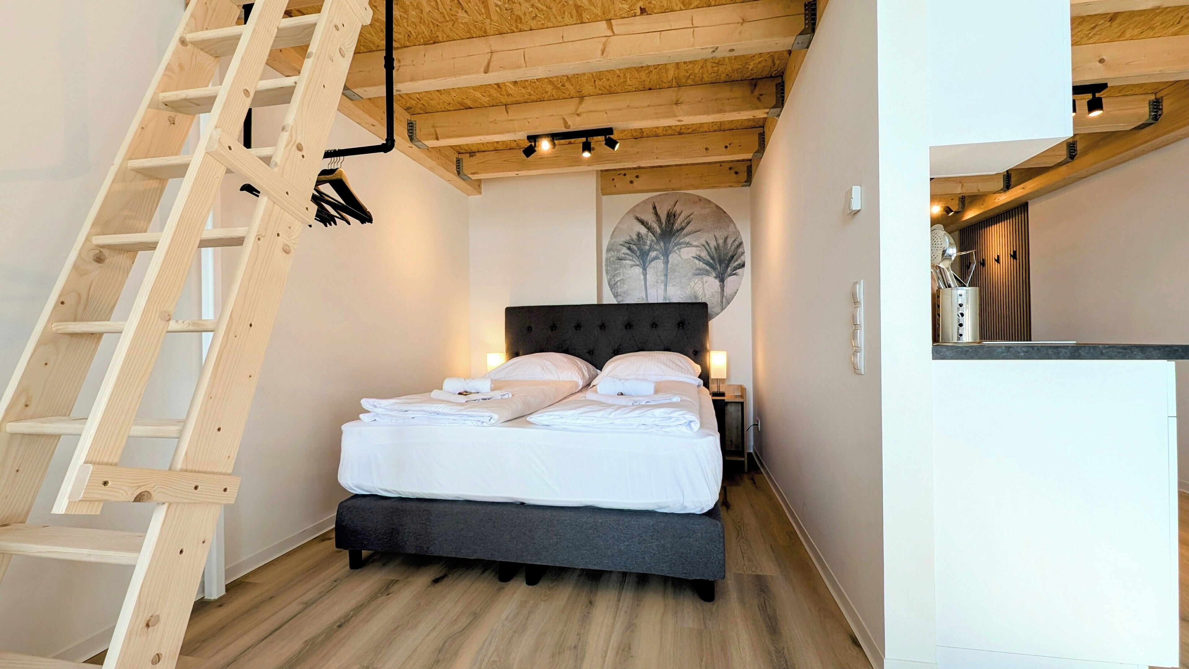 Quarto com cama, escada de madeira e um quadro na parede.