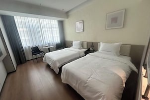 Quarto de hotel com duas camas, uma mesinha, uma cadeira e uma janela com cortinas.