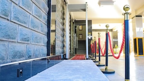 Um hall de hotel com uma recepção de mármore, divisória de vidro e um tapete vermelho que leva a uma escadaria.