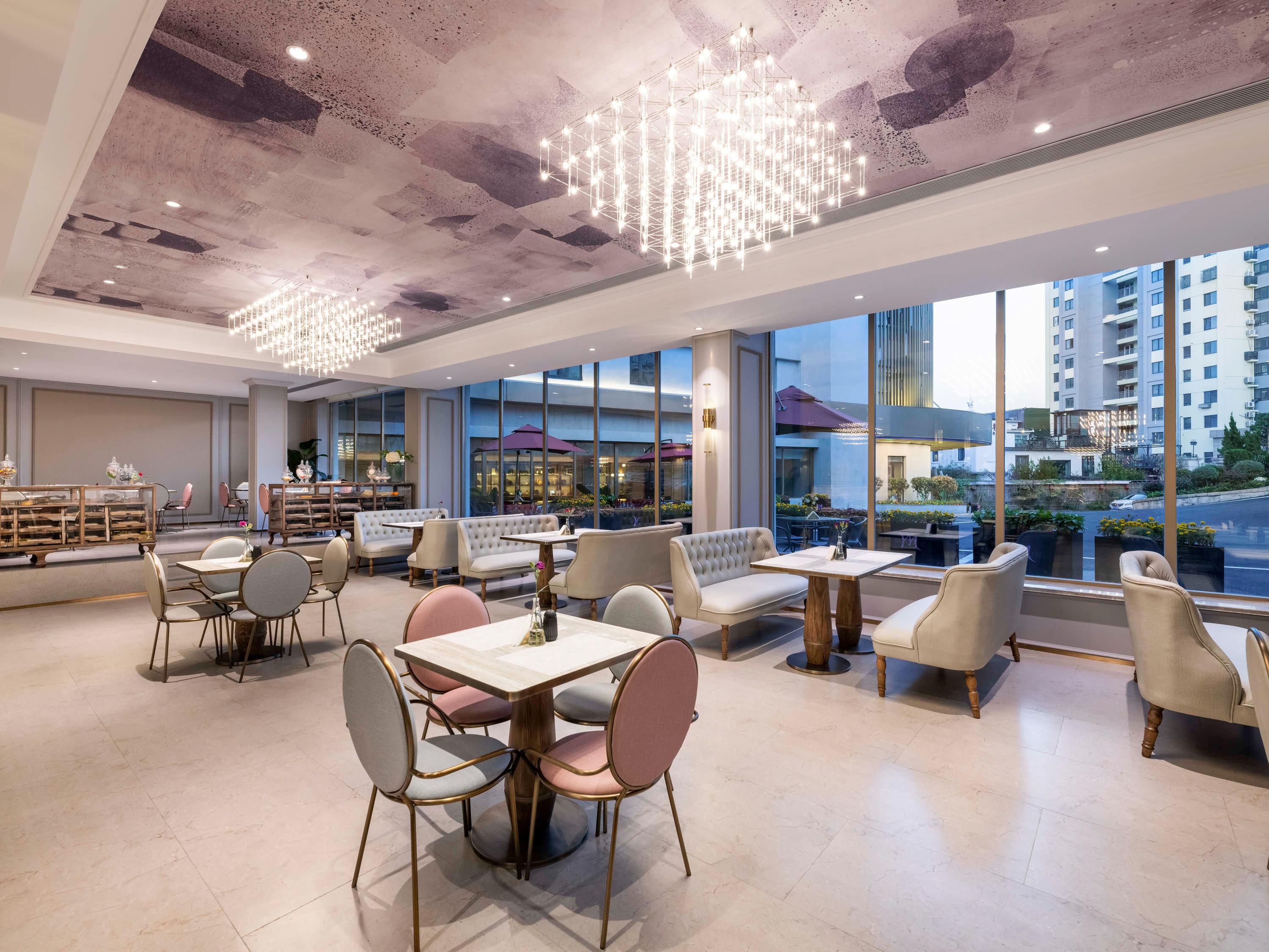 Uma sala de jantar moderna com pé direito alto, lustres e grandes janelas com vista para a cidade.