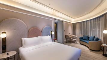 Quarto de hotel moderno com uma cama grande, área de estar com sofá e cadeiras, uma mesa pequena e uma área de refeições separada.