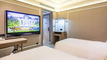 Quarto de hotel com uma cama, uma mesa com cadeira, uma televisão, um espelho e uma porta que dá para outro espaço.