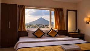 Quarto de hotel com cama, mesa de cabeceira, espelho e janela com cortinas.