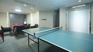 Uma sala de conferência com mesa de pingue-pongue, cadeiras, uma mesa com toalha vermelha e uma porta com painel de vidro jateado.