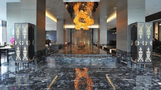Um hall com piso de mármore, um lustre central e decoração simétrica em ambos os lados.