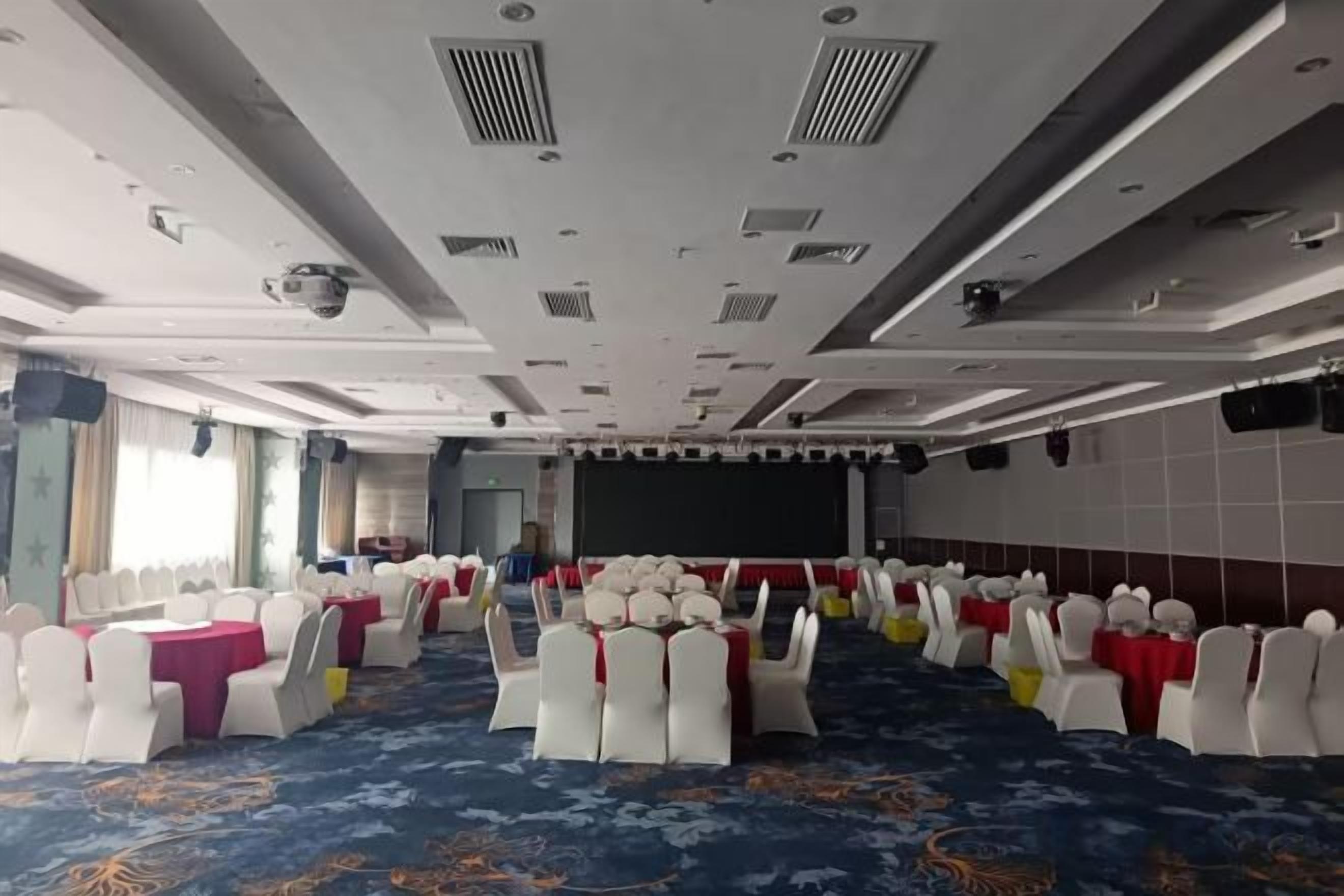 Uma sala de conferências com fileiras de cadeiras brancas, um palco e uma tela grande.