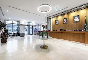 Uma área de recepção moderna com uma mesa redonda de vidro, um balcão de atendimento e retratos emoldurados na parede.