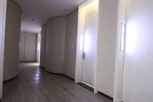 Um corredor com portas à direita, piso de madeira e iluminação embutida.