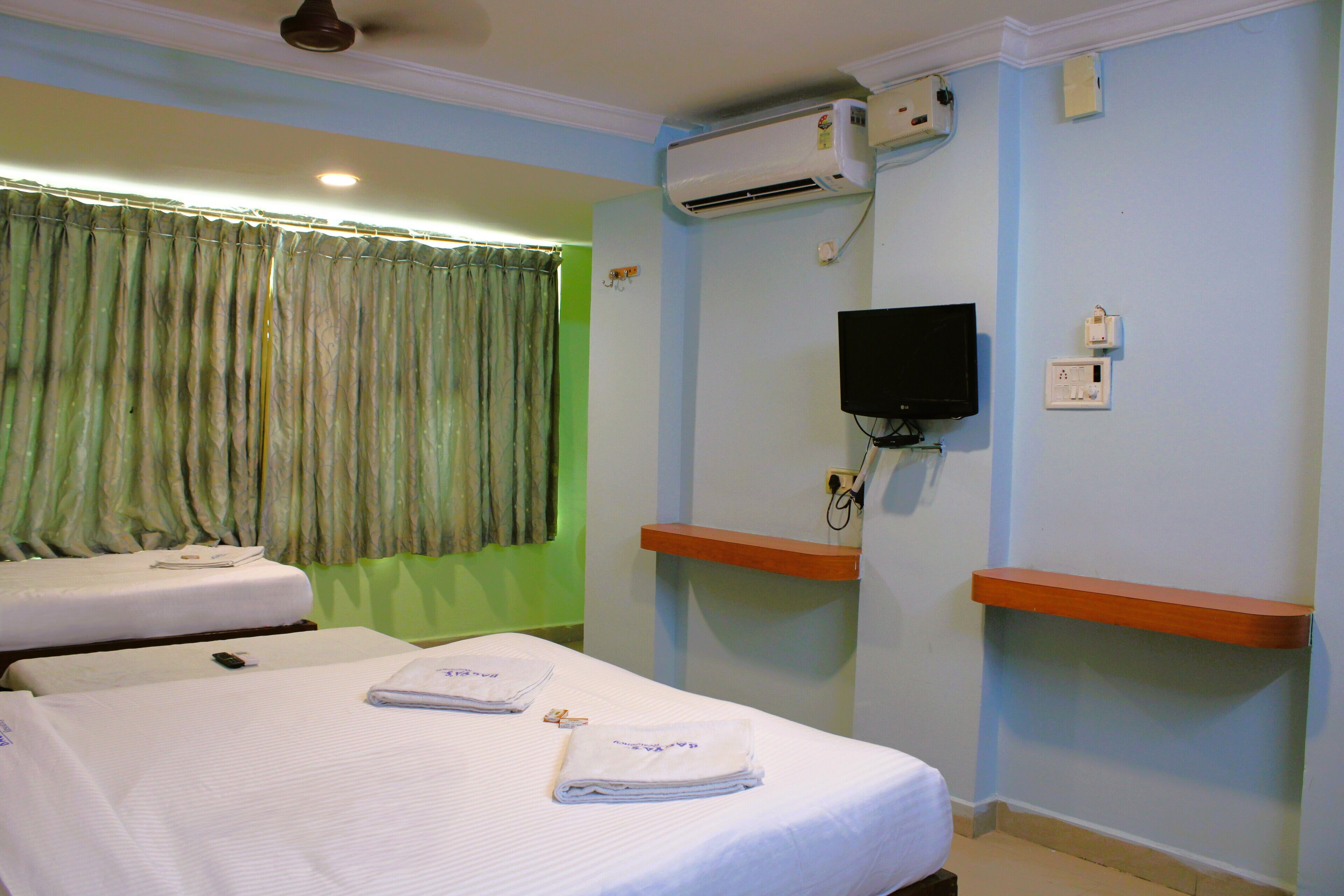 Quarto de hotel com duas camas, televisão, aparelho de ar condicionado e cortina verde.