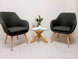 Duas poltronas pretas com pés de madeira, uma mesa de vidro com base de madeira e um vaso de plantas sobre a mesa.