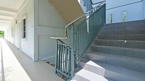 Escadaria coberta ao ar livre, com corrimão de metal, que leva a um edifício com fachada clara.